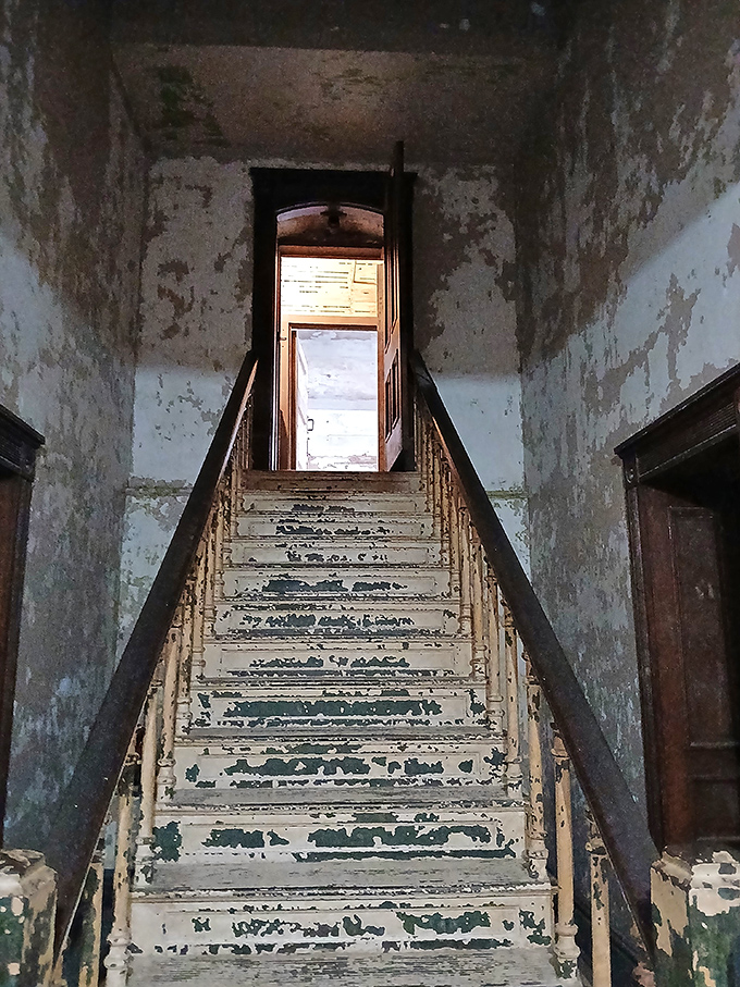 Peeling paint and worn treads tell silent stories on this staircase. Each step represents another boundary between freedom and confinement in this limestone labyrinth.