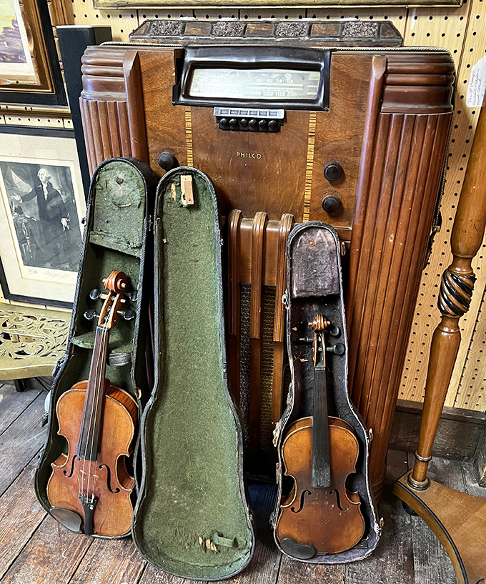 A vintage Philco radio stands sentinel beside violin cases, silent witnesses to decades of melodies now waiting for new hands.