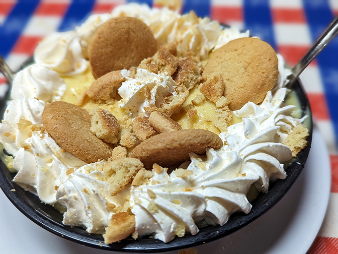 A decadent homemade banana pudding crowned with whipped cream and vanilla wafers awaits on the iconic red and white checkered tablecloth. It's a perfect way to end a hearty meal.