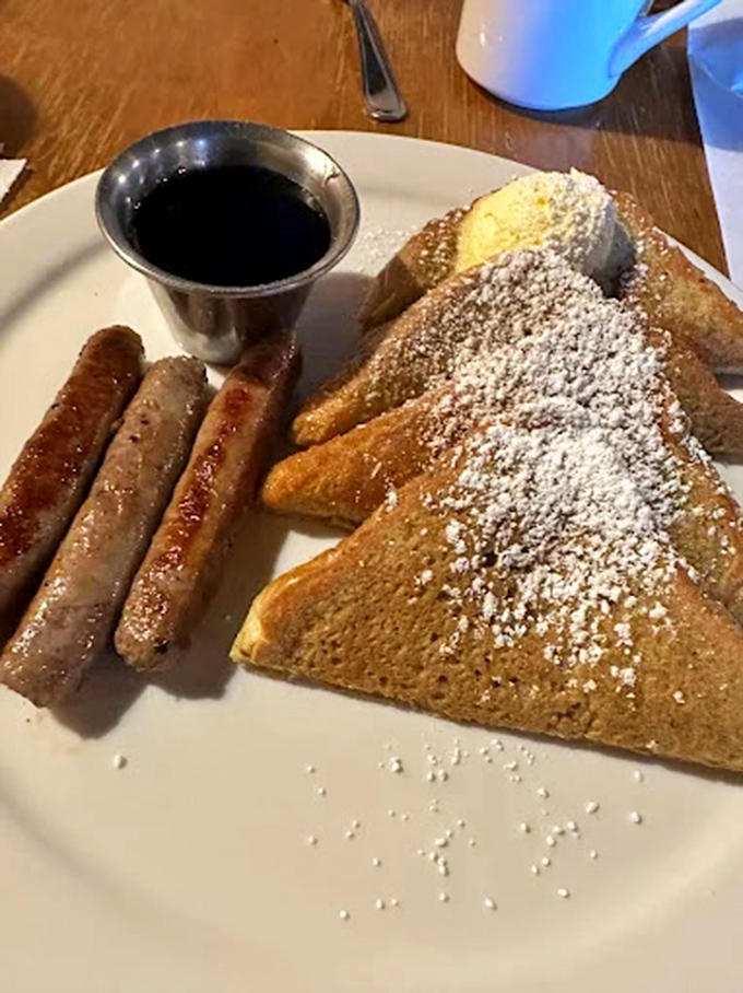 French toast dusted with powdered sugar alongside perfectly browned sausage links &ndash; breakfast nirvana achieved! The metal syrup pitcher is a nostalgic touch rarely seen anymore.