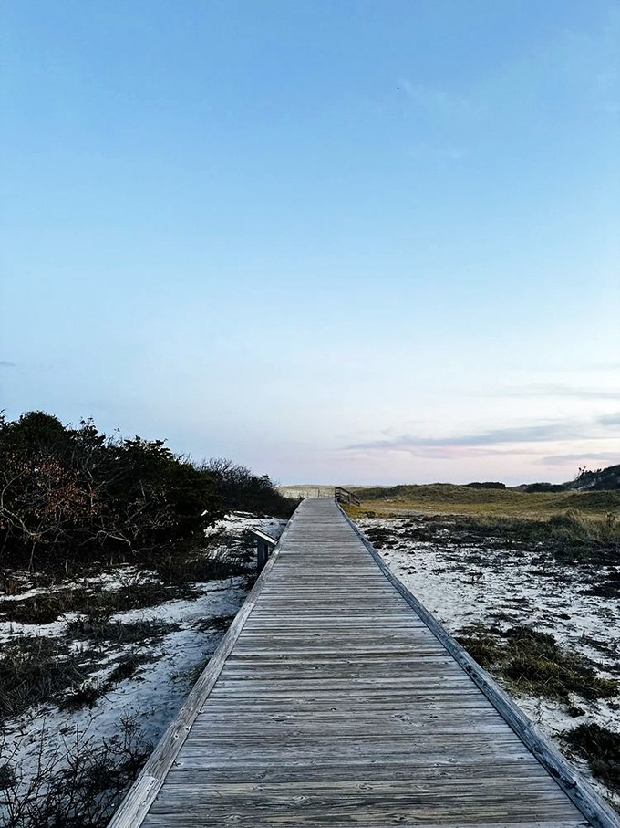 As daylight fades, the boardwalk becomes a pathway to tranquility, cutting through the winter-kissed coastal landscape like a weathered wooden ribbon.