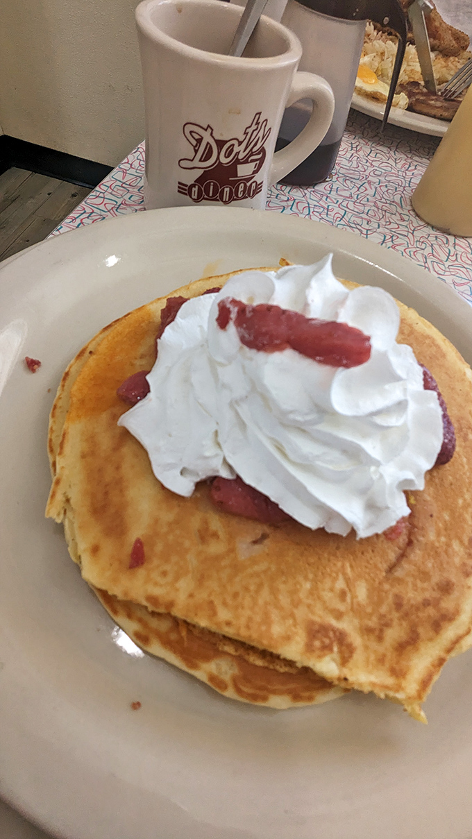 Breakfast bliss in its purest form: golden pancakes crowned with whipped cream and strawberries, paired with that iconic Dots Diner mug of steaming coffee.