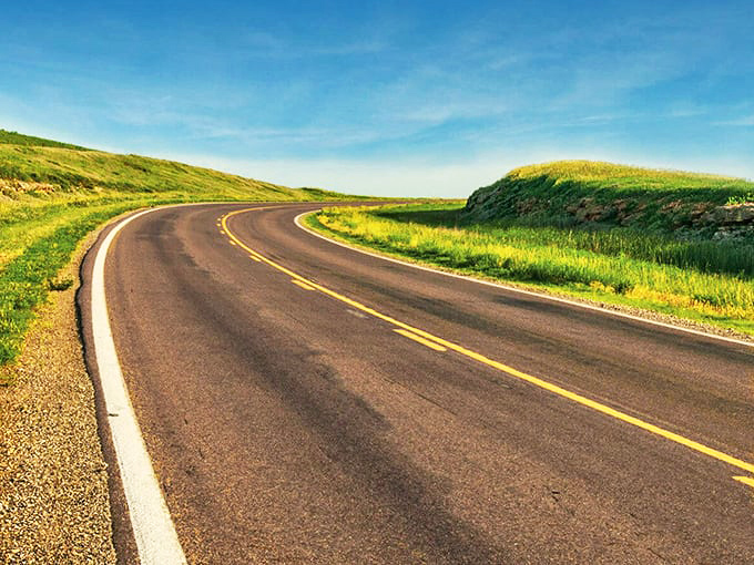 The winding road seems to challenge gravity itself, rising and falling with the ancient rhythm of the hills.