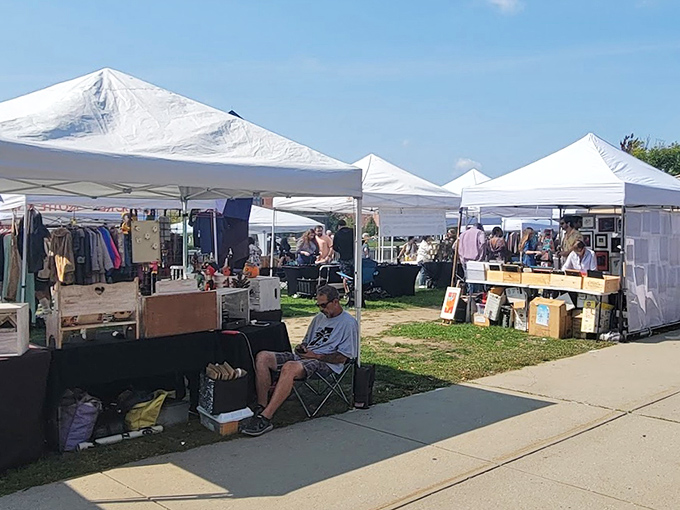 White tents line the outdoor market where vendors display clothing, collectibles, and handmade items under the bright summer sky.