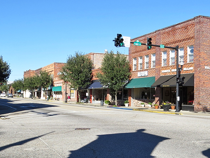Bright morning sunlight casts long shadows across the street, highlighting the row of historic red brick buildings and their colorful awnings in this classic American downtown under a clear blue sky.