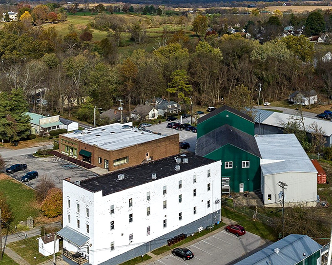 The historic Midway Distilling Company building stands tall in white, surrounded by Kentucky's autumn palette. Where bourbon history meets small-town present in a landscape that hasn't forgotten its roots.