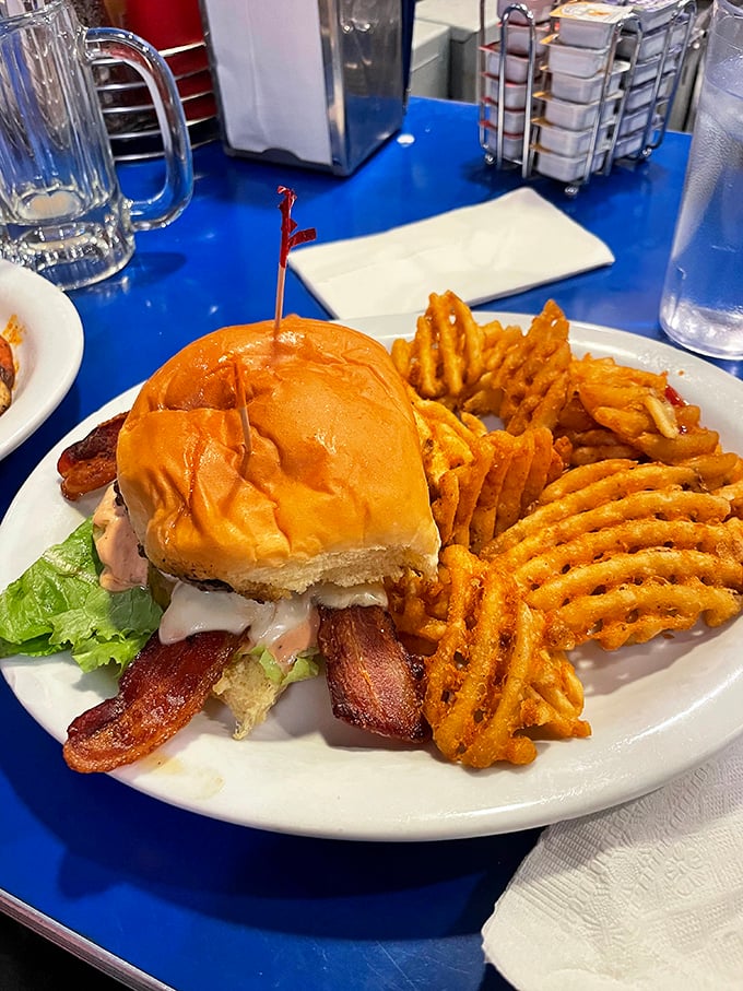 This isn't just a sandwich; it's architecture with purpose. Golden waffle fries stand guard beside a burger that demands a strategic approach to consumption.