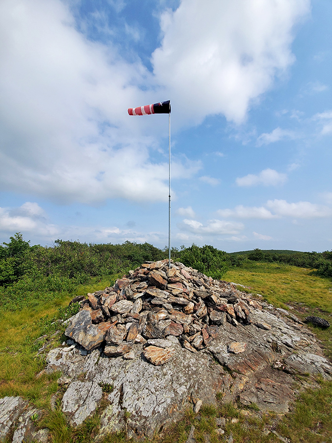 Someone got the rock-stacking memo! This cairn stands sentinel over rolling hills, topped with a wind sock that's seen more weather than a meteorologist.