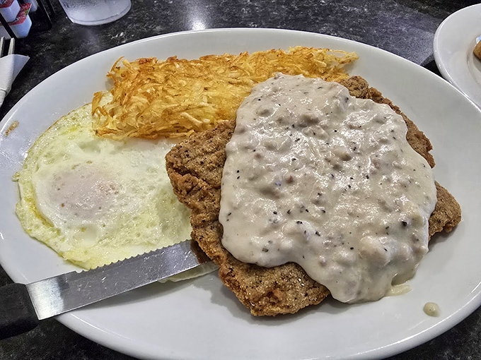 The chicken fried steak arrives like a heavyweight champion, draped in creamy gravy with a sunny-side egg standing guard nearby.