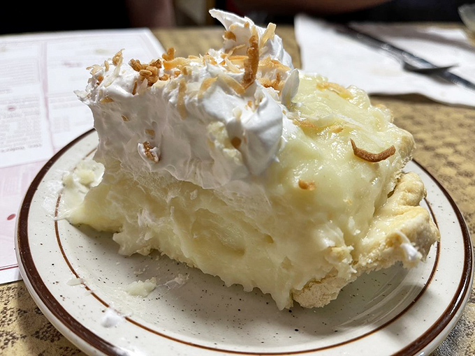 Coconut cream pie standing tall like a delicious skyscraper, defying gravity and dietary restraint with equal measure.