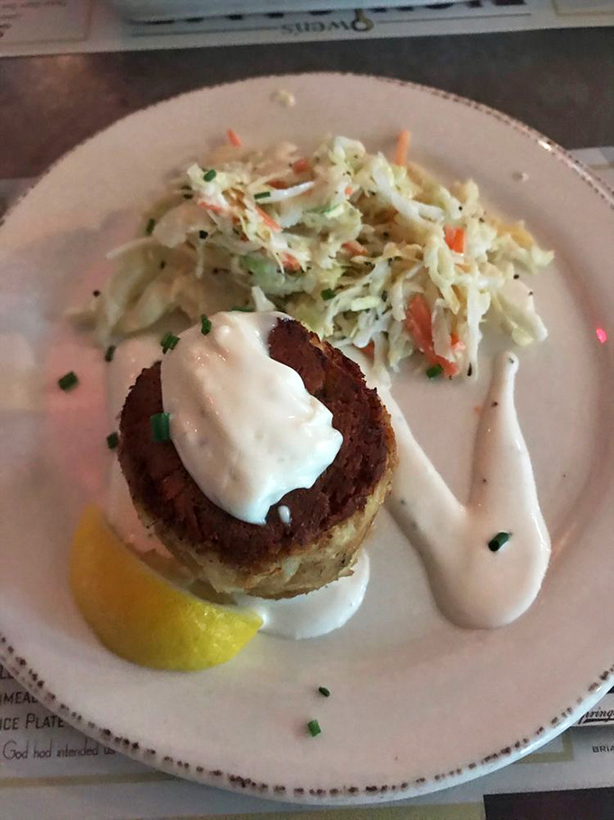 The crab cake arrives like a golden crown atop its throne, accompanied by coleslaw that's actually worth eating&mdash;a rare culinary achievement indeed.