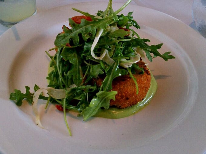 This isn't just a crab cake; it's a golden-crusted island of sweet crab meat surrounded by a sea of peppery arugula and verdant sauce.