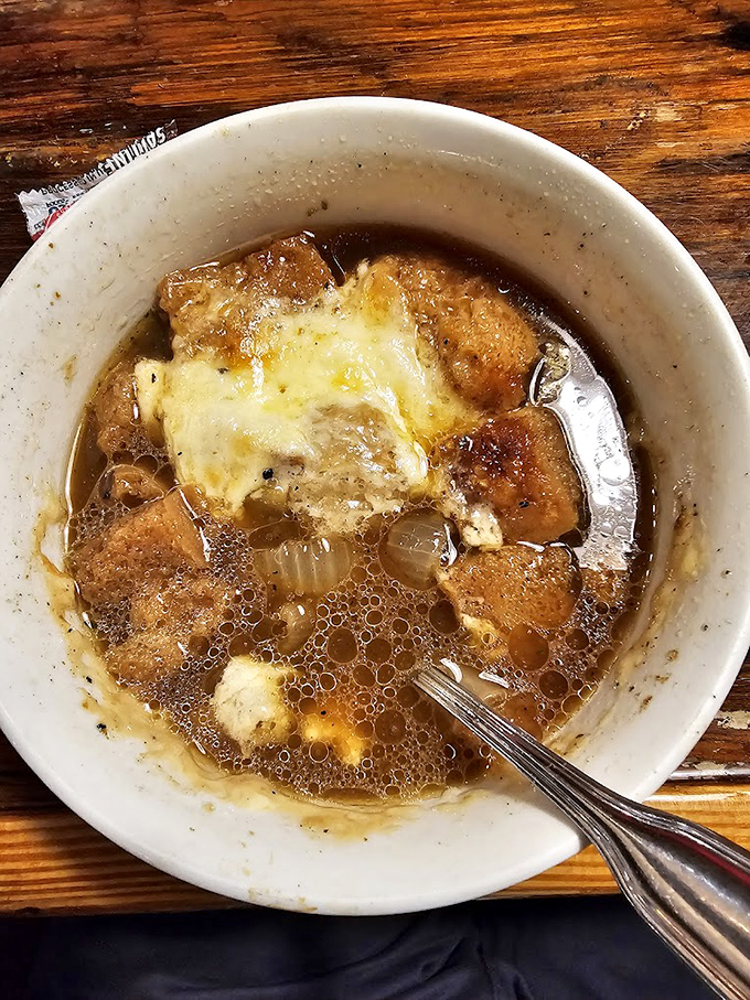 The French onion soup arrives like a bubbling cauldron of comfort, the melted cheese stretching skyward as if reaching for culinary heaven.