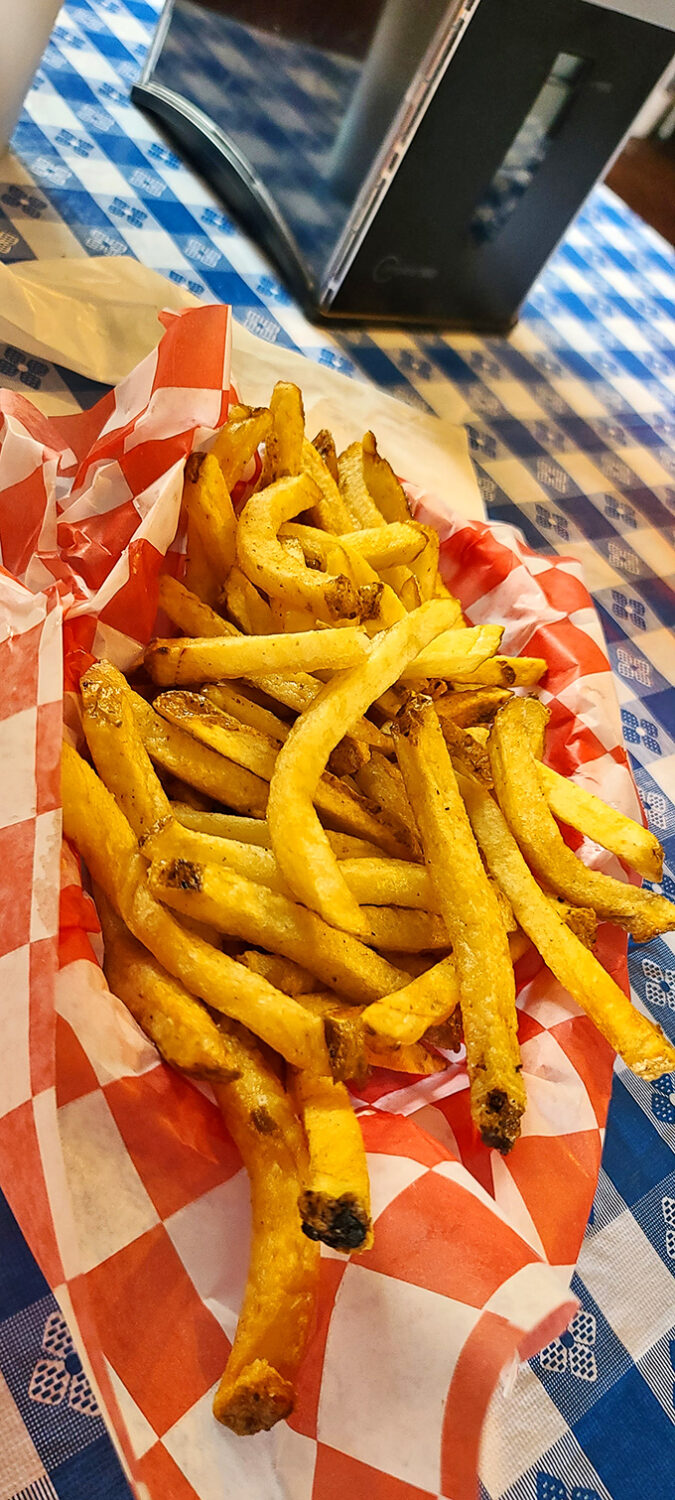 Hand-cut fries at Alamo Springs Caf&eacute; &ndash; golden, crispy perfection served in classic red checkered paper on a blue gingham tablecloth.