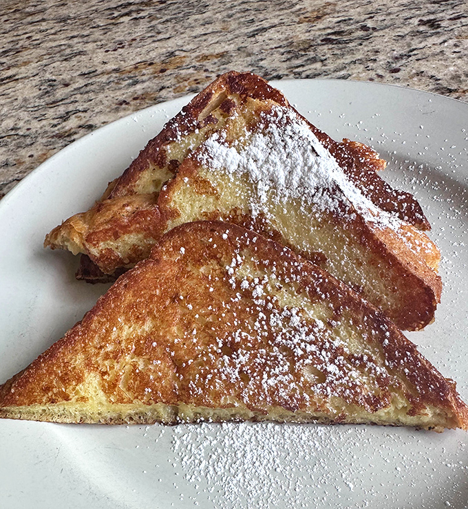 French toast dusted with powdered sugar like fresh snow, golden and perfect, waiting for its syrup bath.