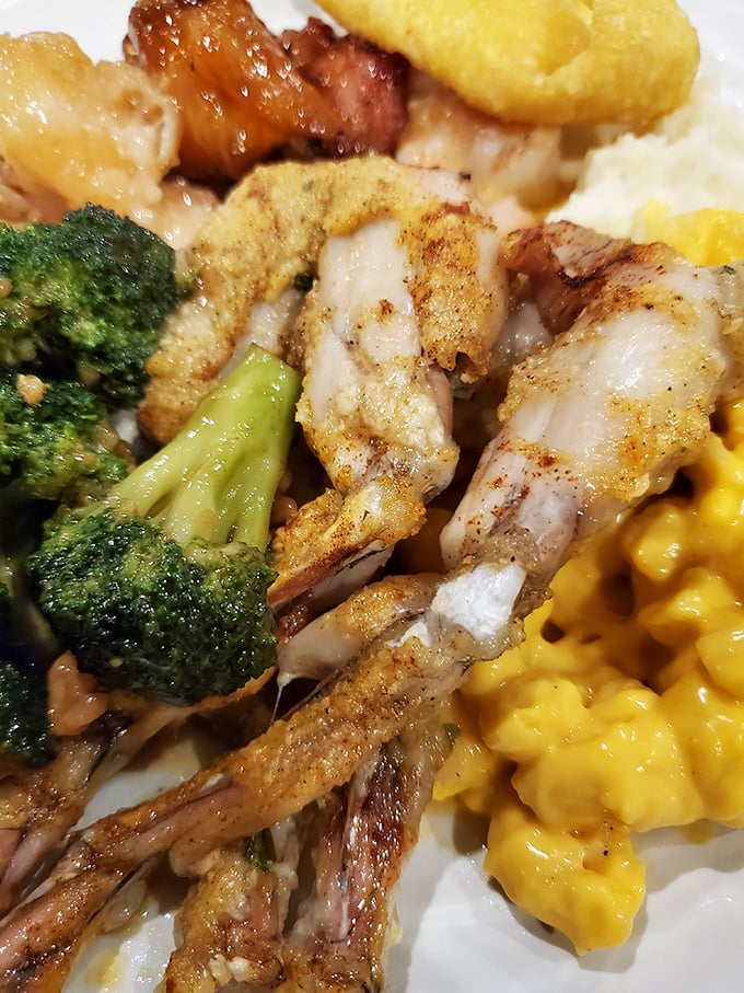A plate that tells the whole story: golden-seasoned frog legs cozied up next to broccoli and mac & cheese &mdash; the buffet equivalent of &lsquo;having your cake and eating it too.