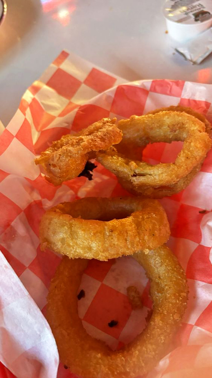Golden onion rings that crunch like autumn leaves, served in a checkered basket of pure nostalgia.