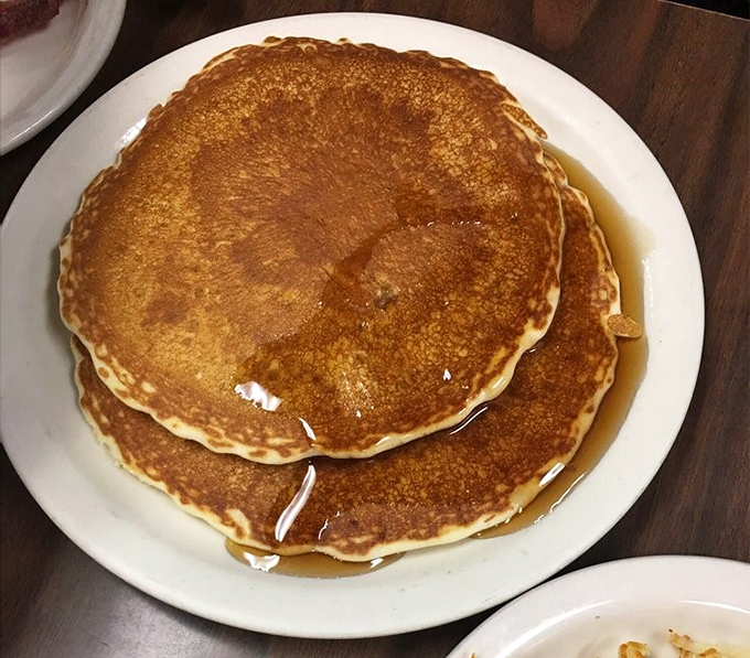 Stack of buttermilk pancakes that could feed a small army, drizzled with syrup perfection.