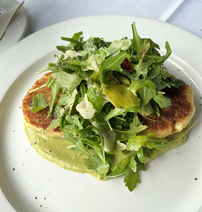 Not just another crab cake &ndash; this golden-crusted beauty sits atop a vibrant green sauce that whispers, "Yes, you made the right choice."