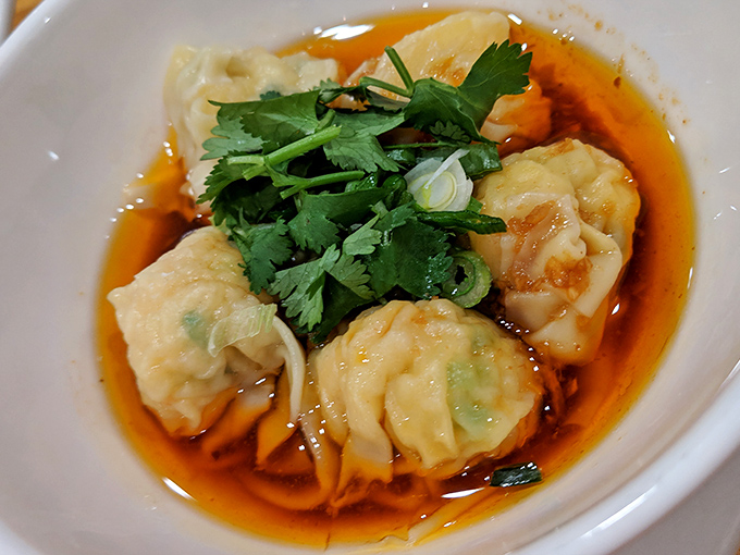 Spicy shrimp wontons nestle in a pool of crimson oil, crowned with cilantro like tiny flavor pillows.