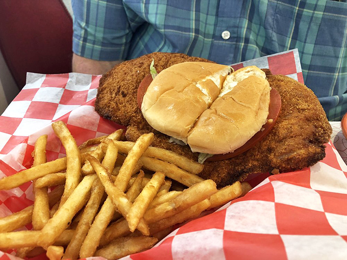 This breaded tenderloin sandwich threatens to escape its bun entirely. Golden fries stand at attention, ready for their supporting role in this Midwest classic.