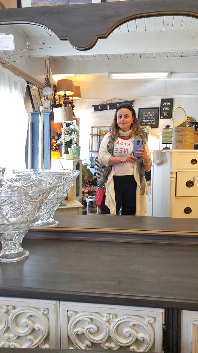 The shop's interior features architectural details like curved wooden accents and vintage cabinetry. Crystal bowls catch the light while furniture pieces await their next chapter.