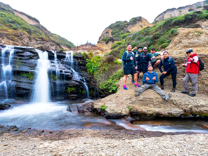 A group celebrates their hiking achievement at the falls, displaying the universal "we made it" pose known to adventurers worldwide.