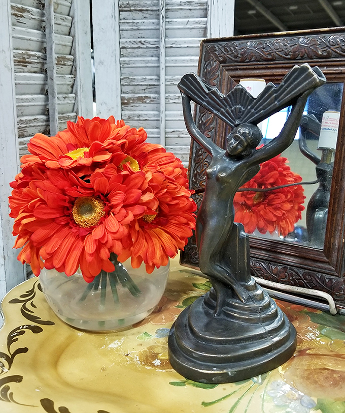 An Art Deco figurine poses elegantly beside vibrant gerbera daisies, creating the kind of vignette that makes you rethink your living room decor.