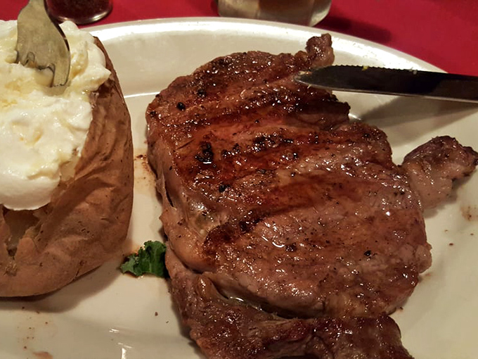 Talk about a hearty steak! This perfectly grilled ribeye, resting next to a loaded baked potato, is a carnivore's dream come true.