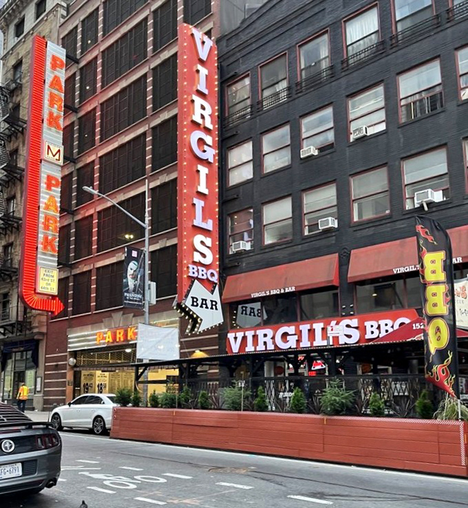 Where barbecue dreams tower high! Virgil's vertical red sign beckons like a meaty lighthouse, guiding hungry souls through Manhattan's concrete jungle to smoky salvation.