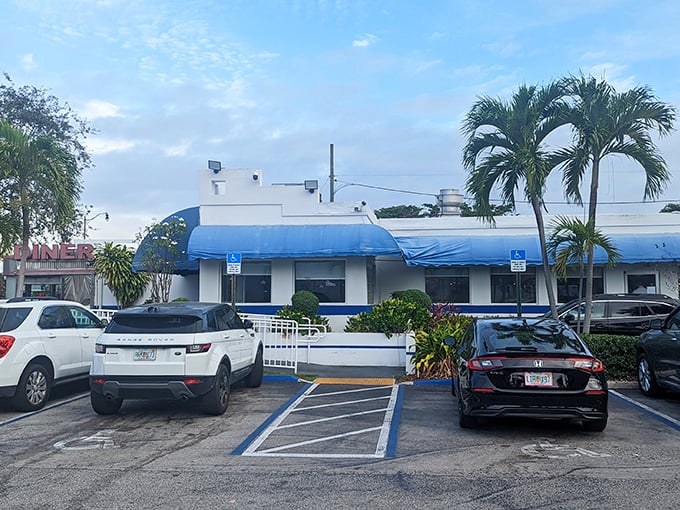 The blue awnings and palm trees frame this retro diner where eggs are cracked with the precision of a breakfast symphony conductor.