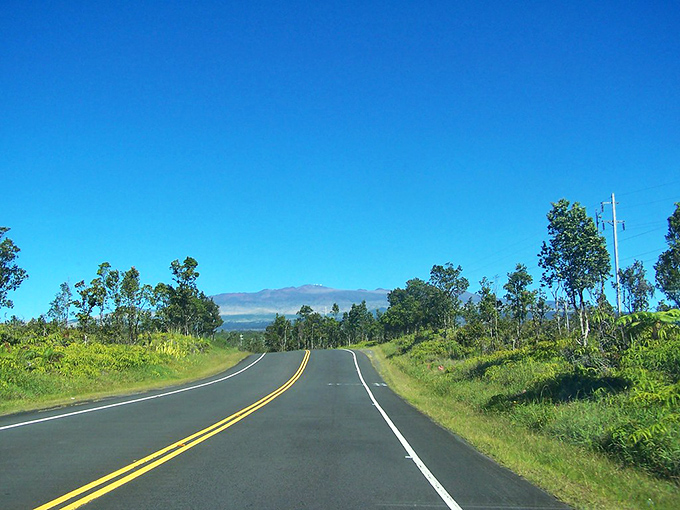 The stairway to heaven has yellow lines! Saddle Road climbs toward Mauna Kea's cloudy crown, delivering tropical vibes with mountain majesty.