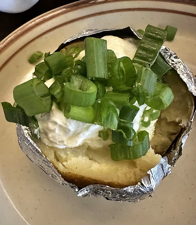 The loaded baked potato arrives like a comfort food superstar. Wrapped in foil with a burst of steam that announces, "I'm worth every calorie you're about to enjoy."