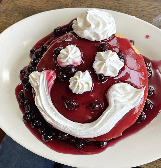 A smiley face pancake topped with blueberry compote and whipped cream &ndash; breakfast with personality that's impossible to eat without grinning back.