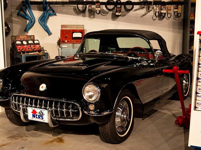 This classic black C1 Corvette sits in a period-correct service station display, transporting visitors to an era when gas station attendants actually cleaned your windshield.