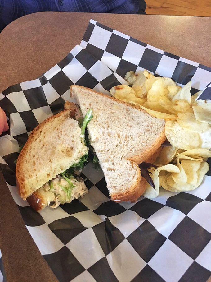 A chicken salad sandwich that doesn't apologize for being simple, served with house-made chips on a checkerboard paper that screams "comfort food royalty."