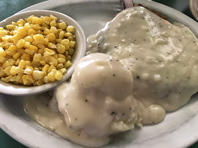 Country comfort on a plate: cream gravy cascades over chicken fried steak like a delicious waterfall, with golden corn standing by for moral support.