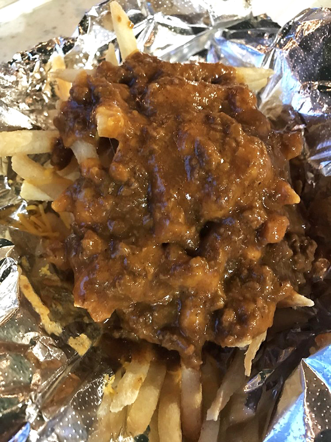 Chili cheese fries: where comfort food reaches its final, glorious form. The aluminum foil cradles this masterpiece like it's protecting the crown jewels of snackdom.