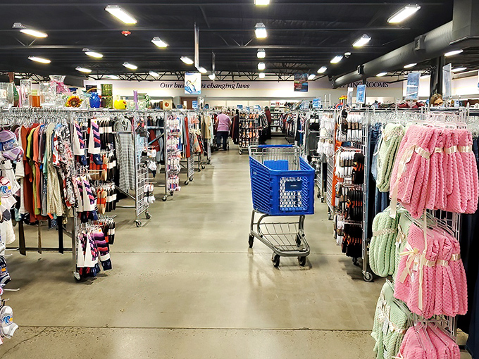 Clothing racks create colorful canyons to navigate. Each garment tells a story—some barely begun, others with chapters of adventures already lived.