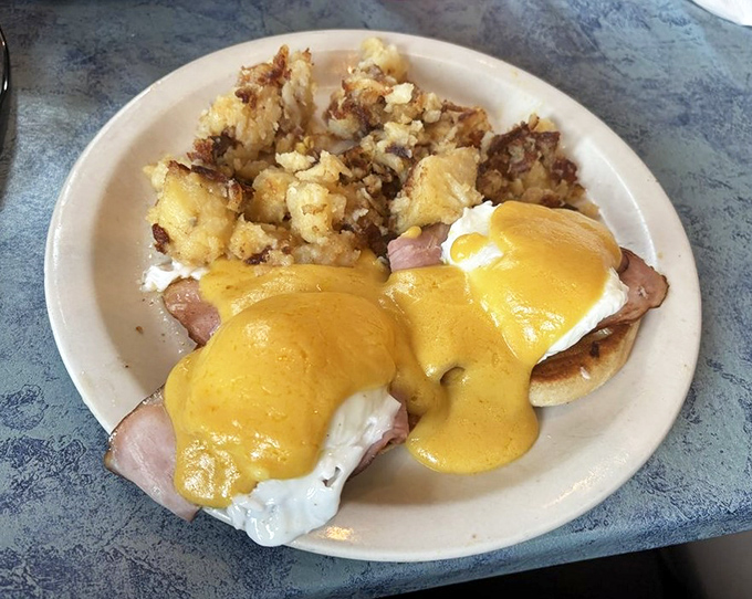 Eggs Benedict with home fries&mdash;where hollandaise sauce cascades like a yellow waterfall of happiness over perfectly poached eggs and ham.