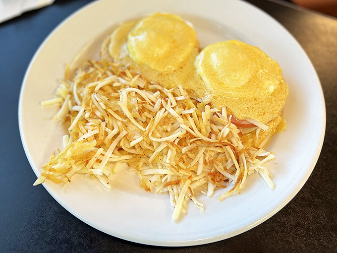 Eggs Benedict with hash browns&mdash;where hollandaise dreams come true. That cheese blanket isn't just garnish; it's commitment to excellence.