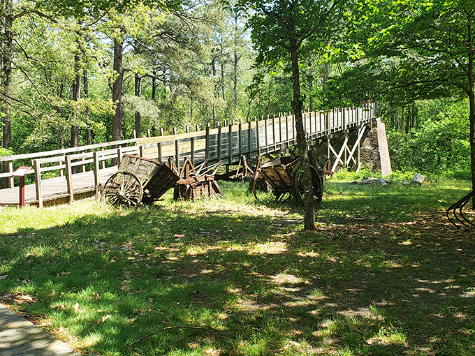 A wooden bridge stretches toward adventure, with antique farm equipment standing guard. History and nature having a friendly chat.
