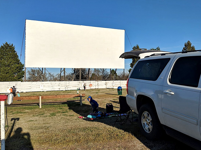Early birds claim prime spots as children sprawl on blankets, mastering the art of pre-movie patience that streaming services have nearly erased from human experience.
