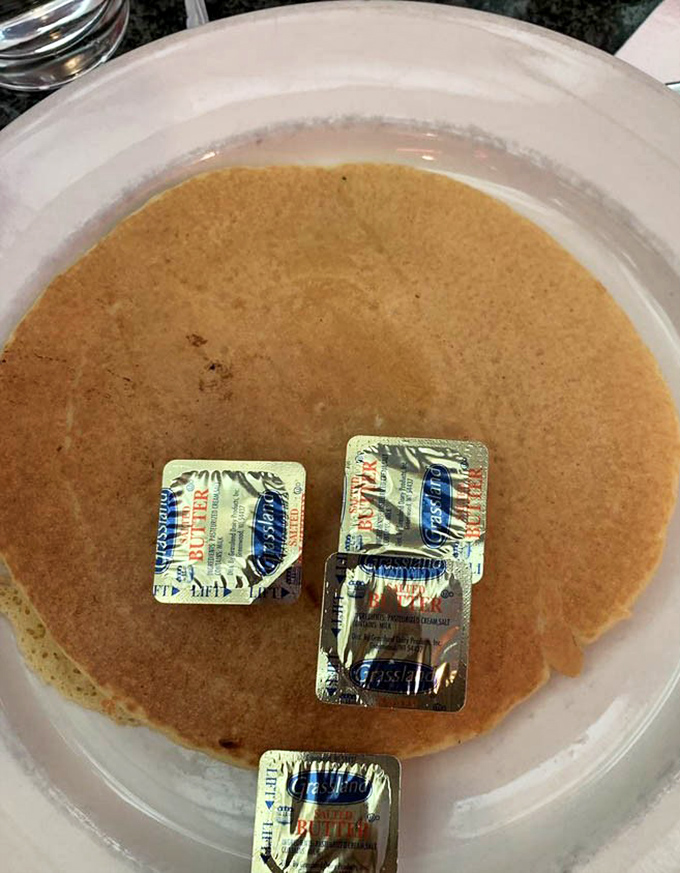 Pancake perfection with butter packets standing by like eager understudies. This golden disc is ready for its maple syrup waterfall moment.