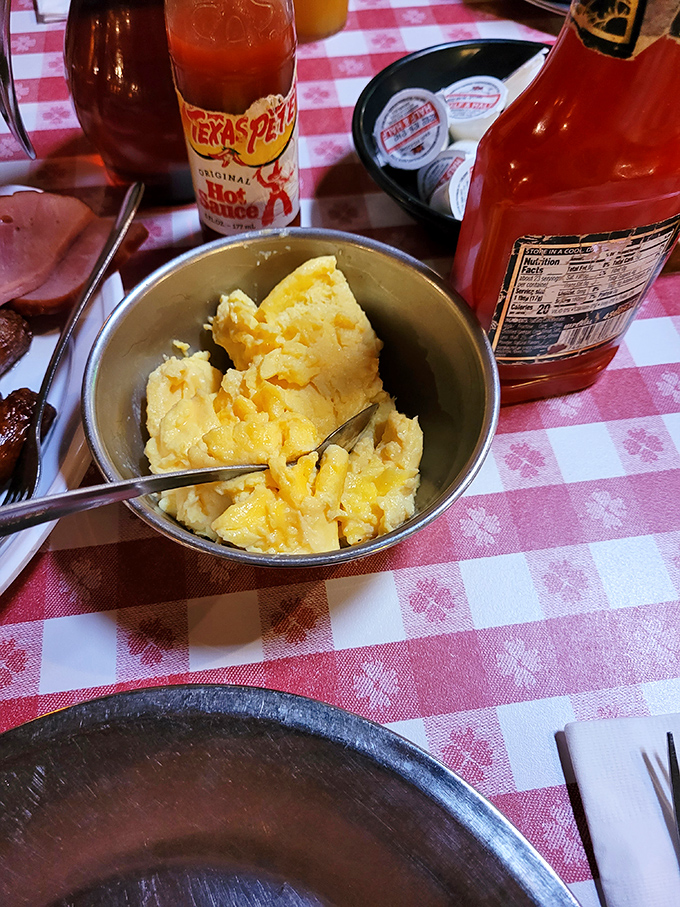 Golden scrambled eggs in a metal bowl, surrounded by hot sauce bottles &ndash; the perfect lumberjack-worthy side to soak up that legendary gravy.