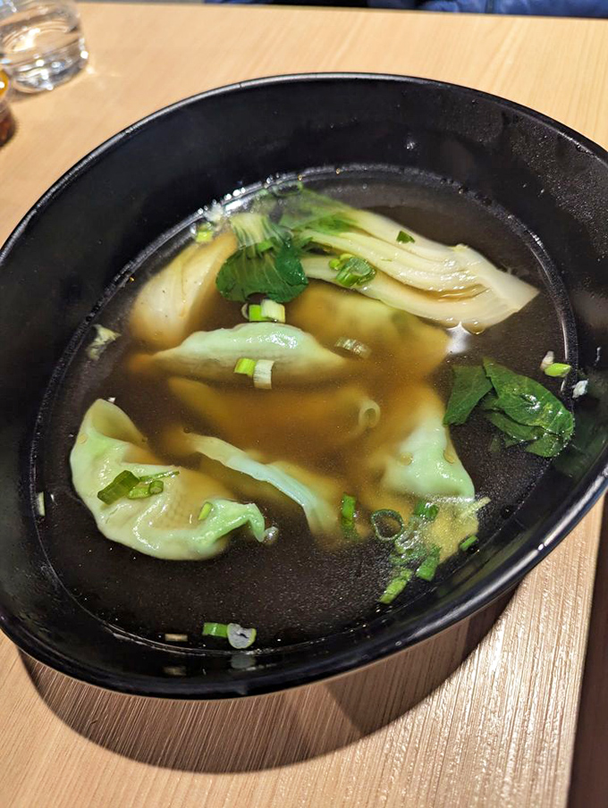 Dumplings swimming in broth like synchronized dancers &ndash; each delicate fold visible through the clear, aromatic soup that warms the soul.