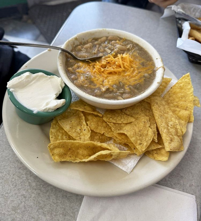 A bowl of white chicken chili soup that would make your grandmother nod in approval, served with chips and a side of Midwest comfort.