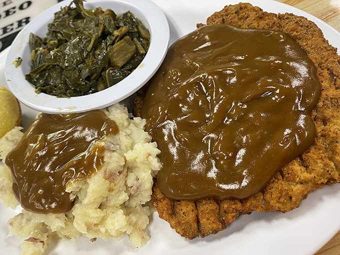 Country fried steak swimming in gravy alongside collard greens and mashed potatoes &ndash; the holy trinity of Southern comfort on a single plate.
