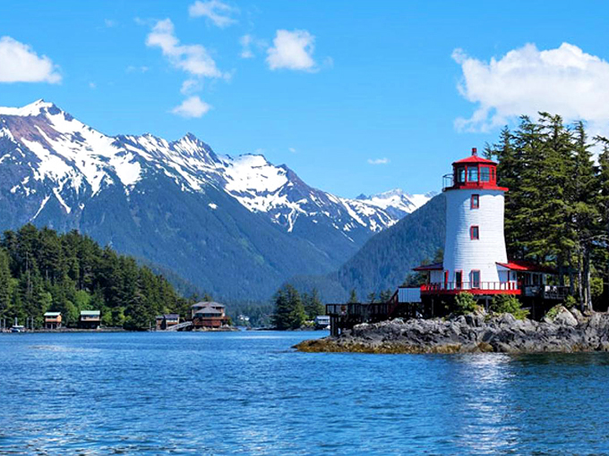 Sentinel Lighthouse stands guard where land surrenders to sea, its red-capped tower a beacon of hope against a backdrop of indifferent mountains.