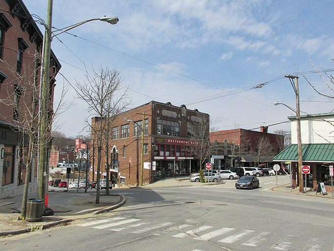 Late morning sun lights up a historic brick downtown intersection, where vintage commercial buildings mark the street corner under a partially cloudy spring sky.